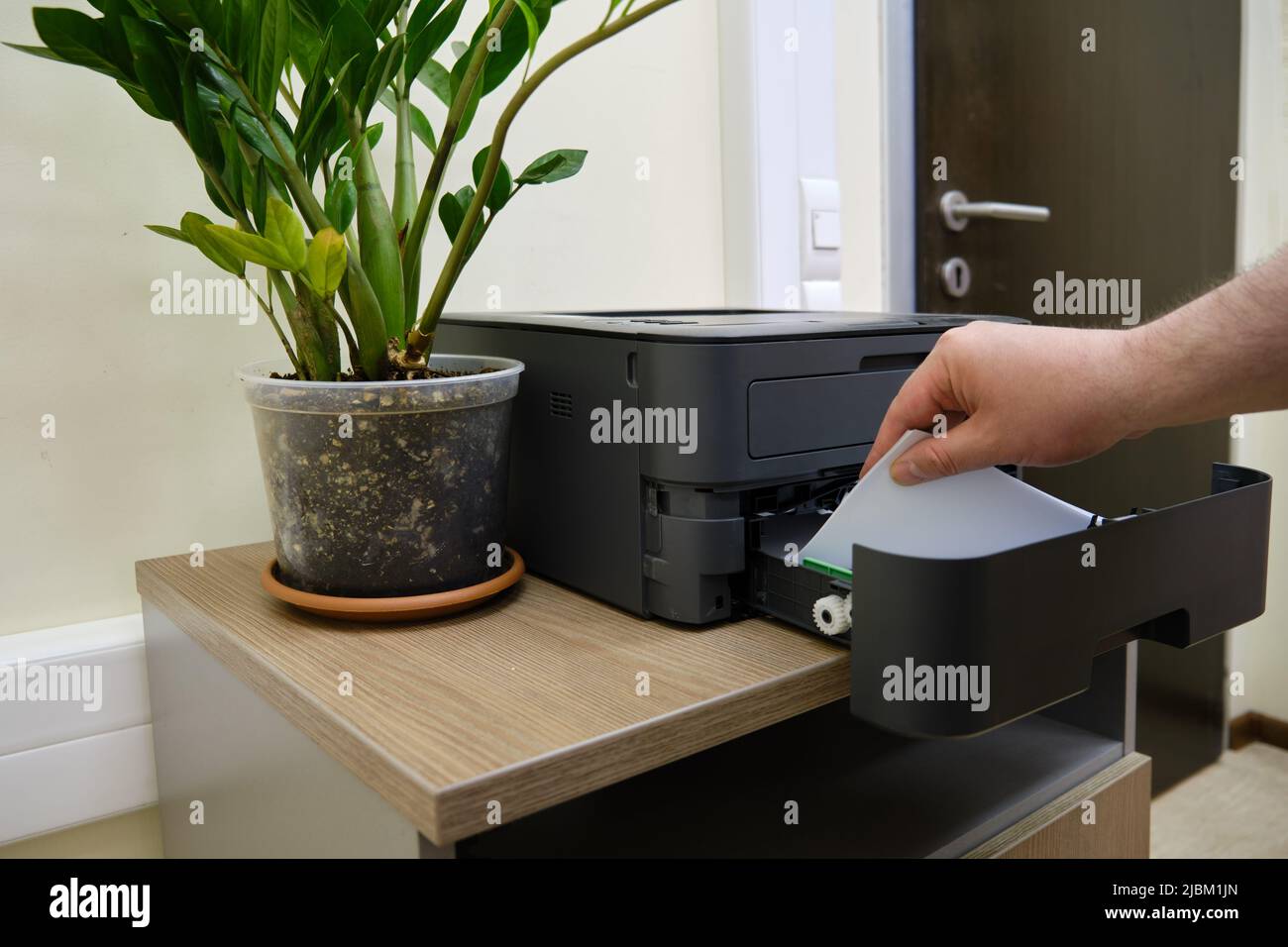 A man hand holds a sheet of paper A4 from a printer in an office room ...