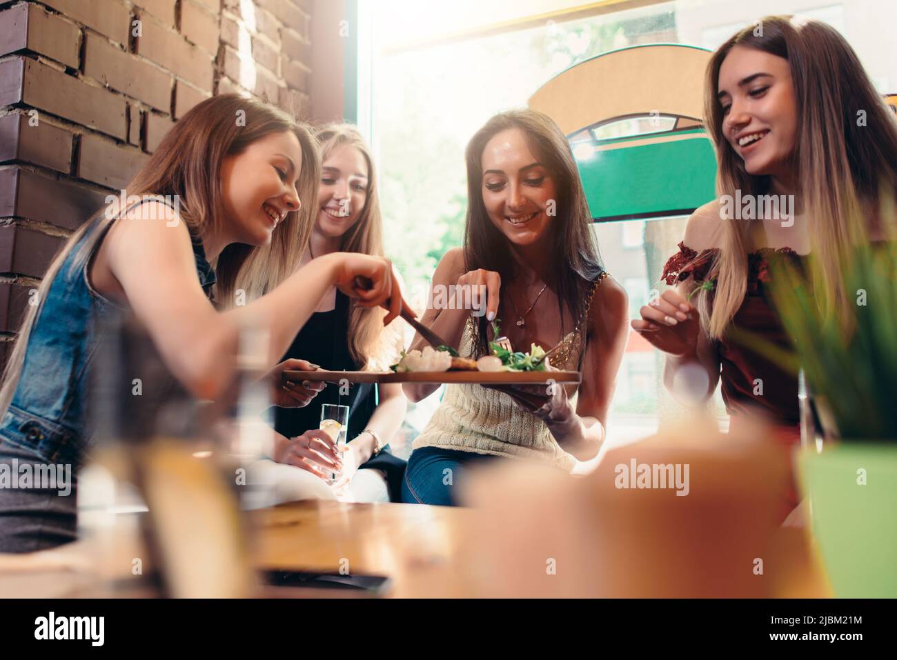Group of laughing pretty young women sharing food sitting at coffee ...