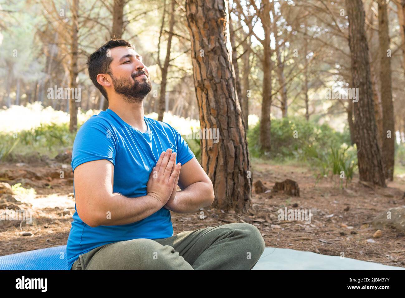 Handsome young adult relaxing practicing meditation sitting on his blue ...