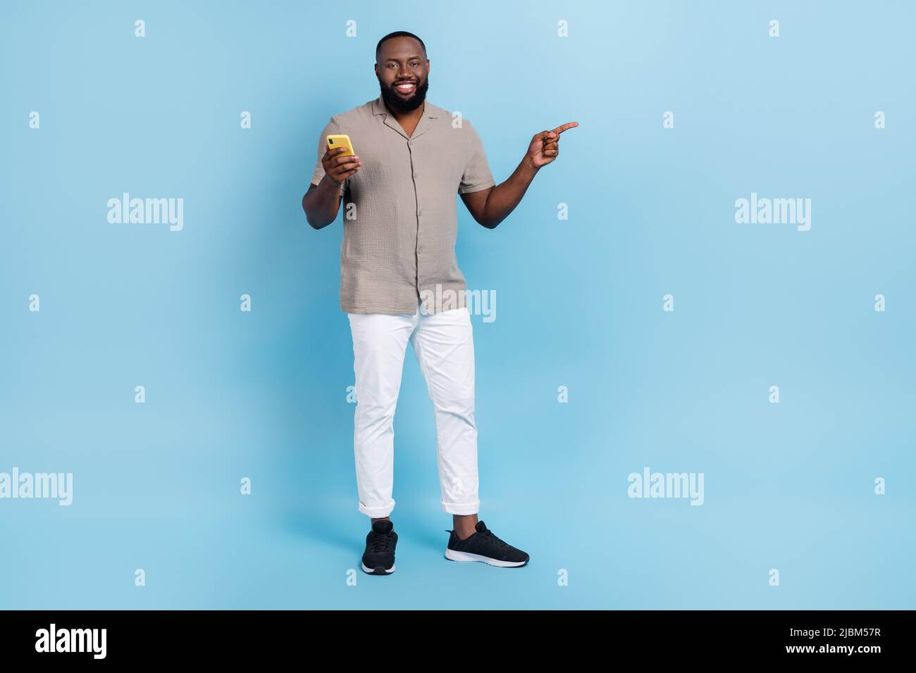 Full length portrait of handsome cheerful guy hold telephone indicate ...