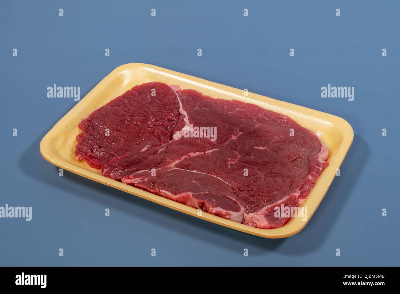 red meat beef in yellow foam board in a blue background Stock Photo - Alamy