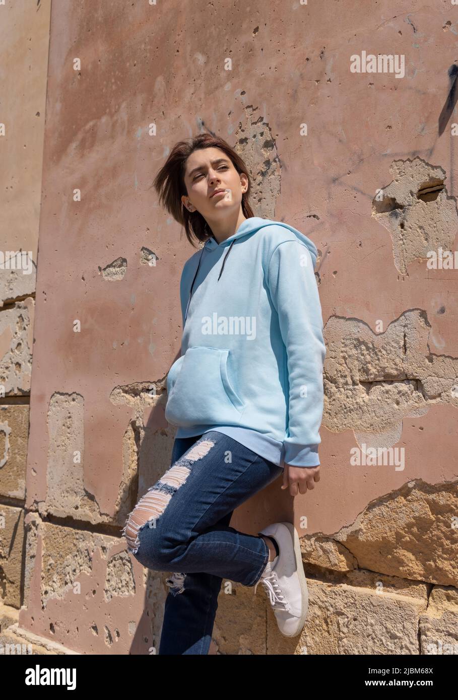 Teenager girl in light blue hoodie nd jeans standing near a ruined wall ...