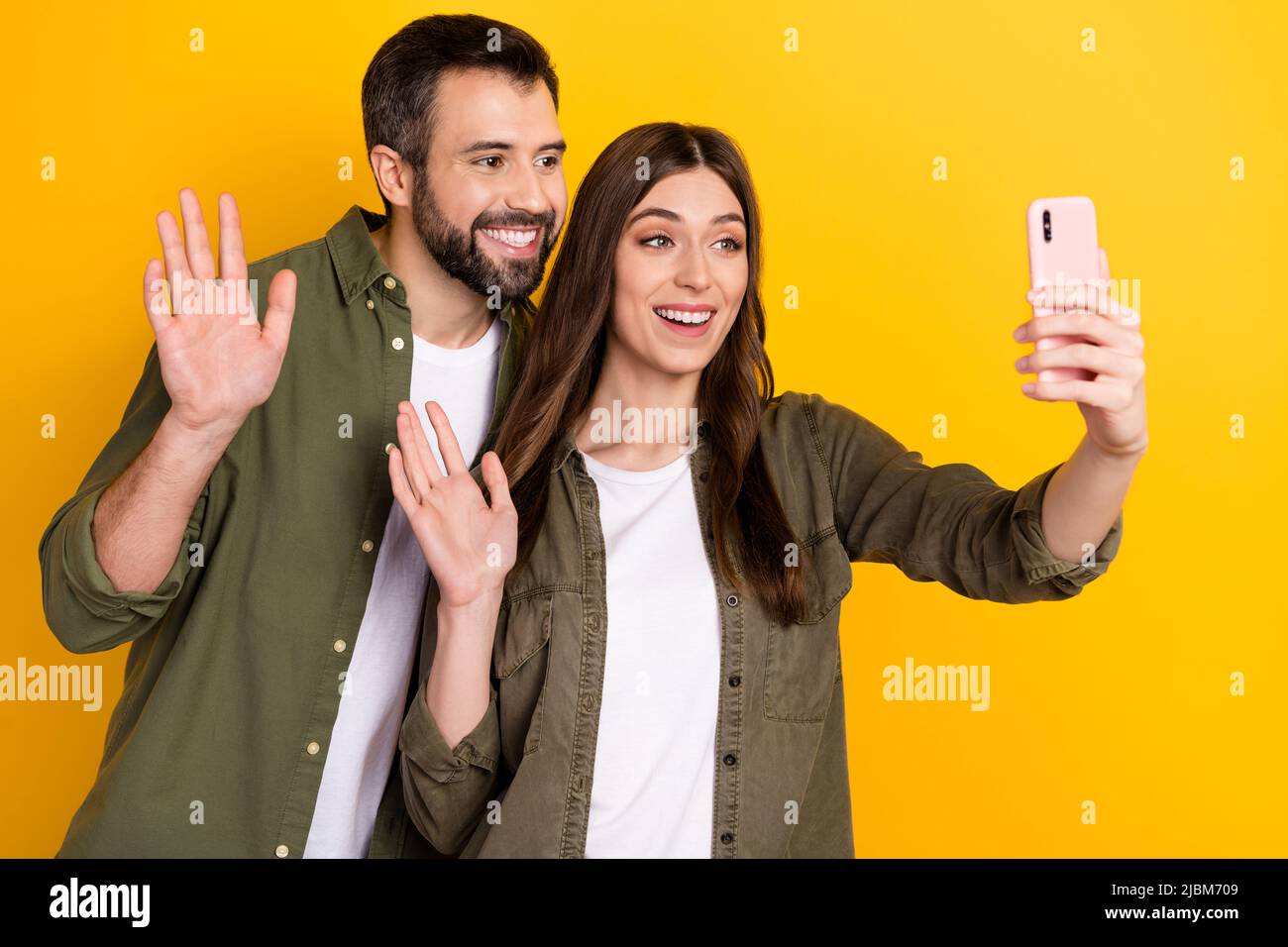 Portrait of attractive cheerful couple using device waving hi hello making selfie isolated over ...