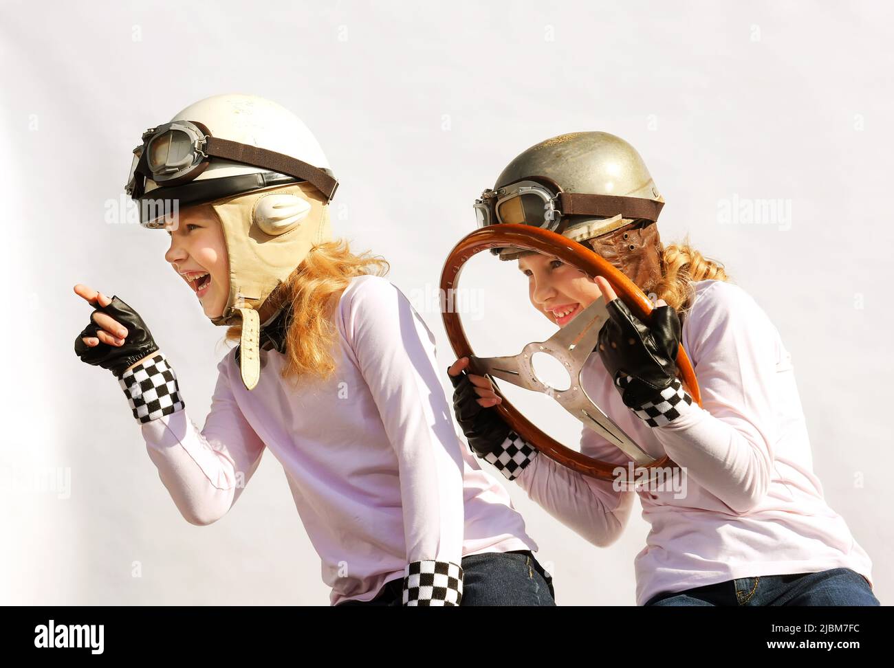 Twin sisters imagine their are driving a sports car. They are wearing ...
