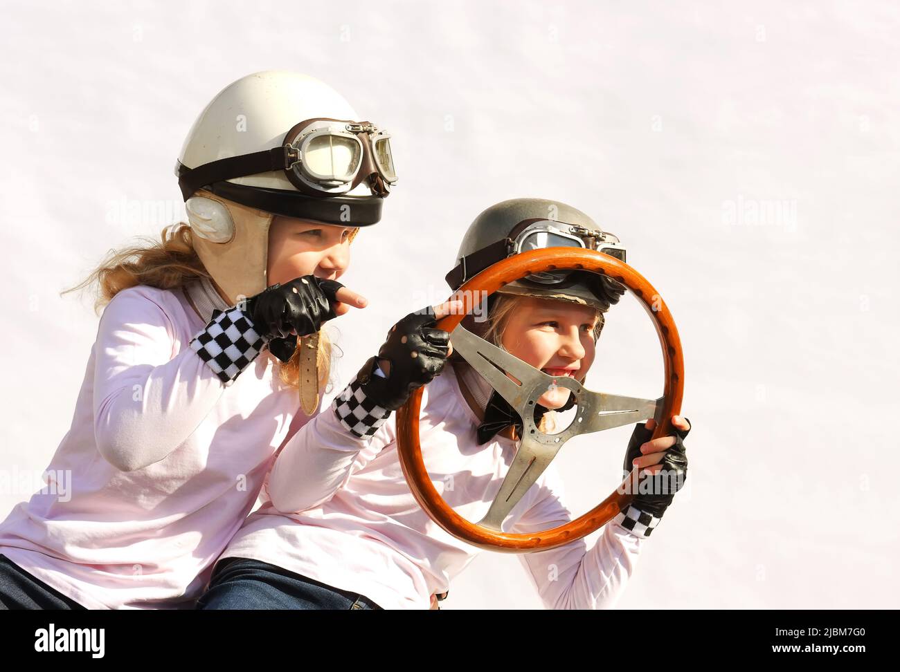 Twin sisters imagine their are driving a sports car. They are wearing ...