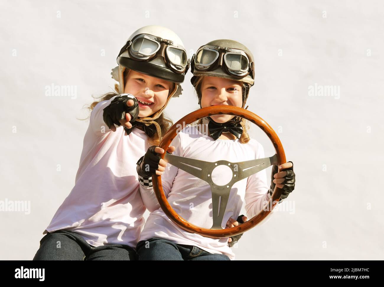 Twin sisters imagine their are driving a sports car. They are wearing ...
