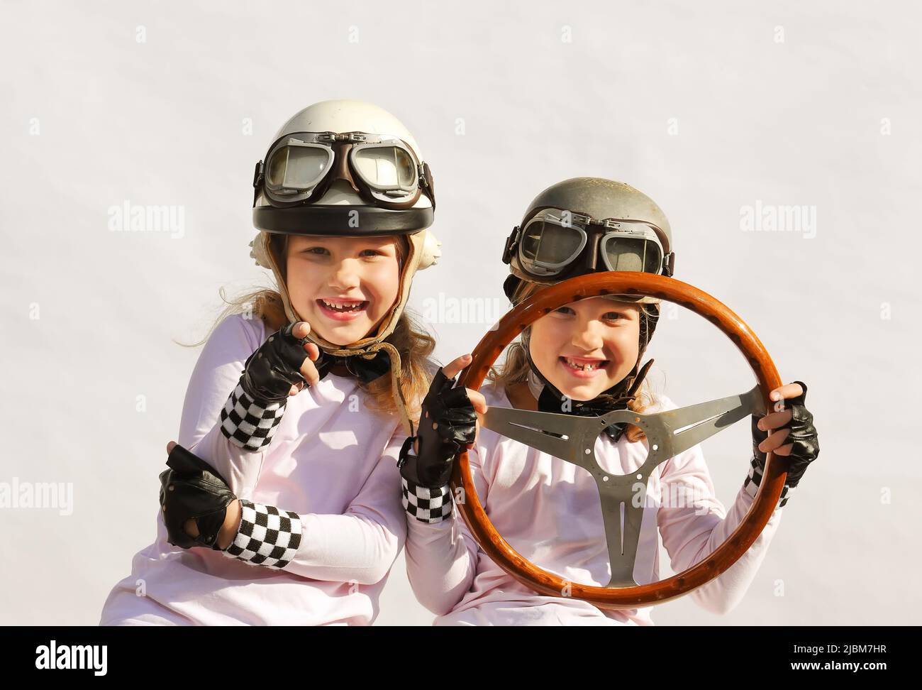 Twin sisters imagine their are driving a sports car. They are wearing ...