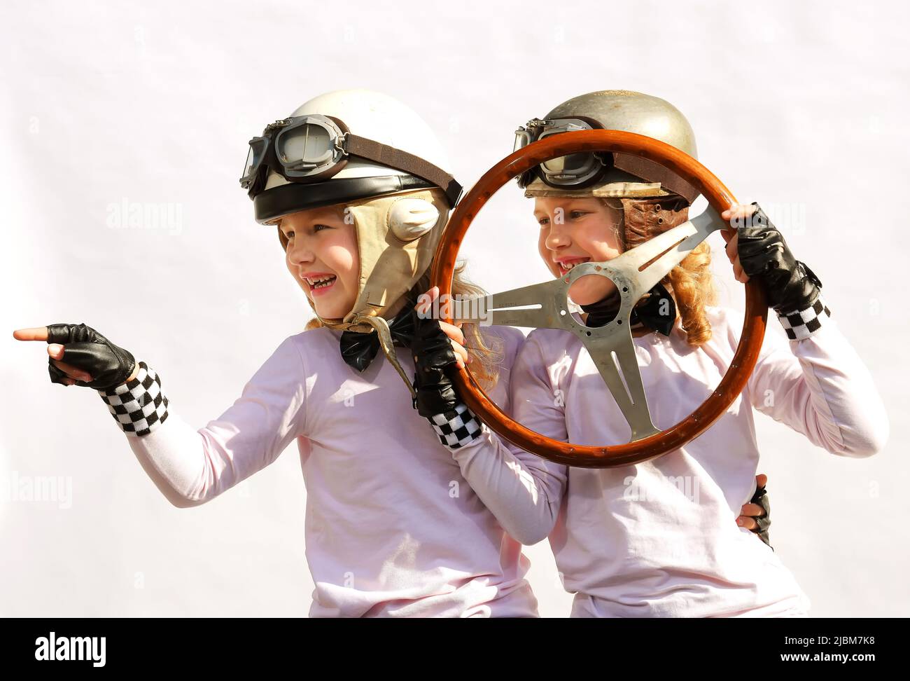 Twin sisters imagine their are driving a sports car. They are wearing ...