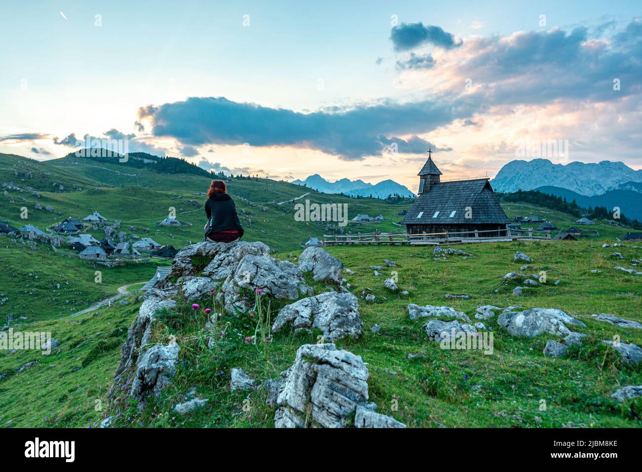 lone traveler sitting on rock, mesmerized by grassland mountains, huts ...