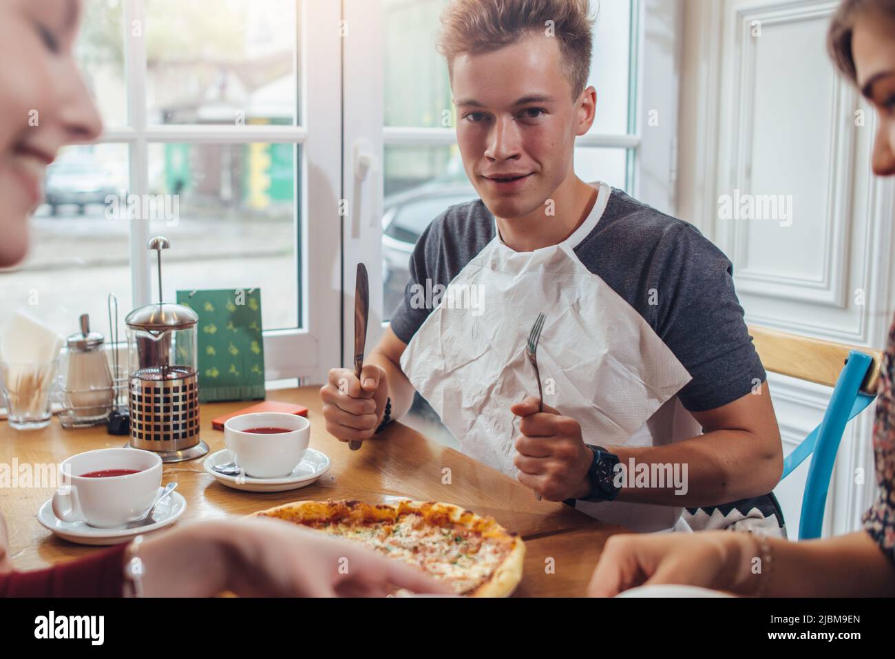 Stylish teenager wearing napkin holding knife and fork ready to eat ...