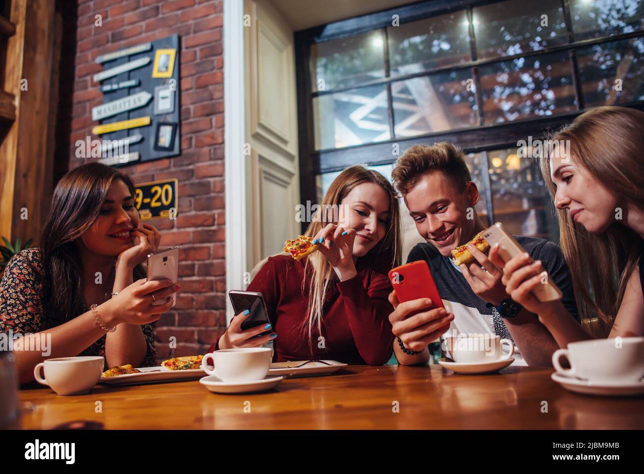 Young people using their mobile phones sitting around the table having ...