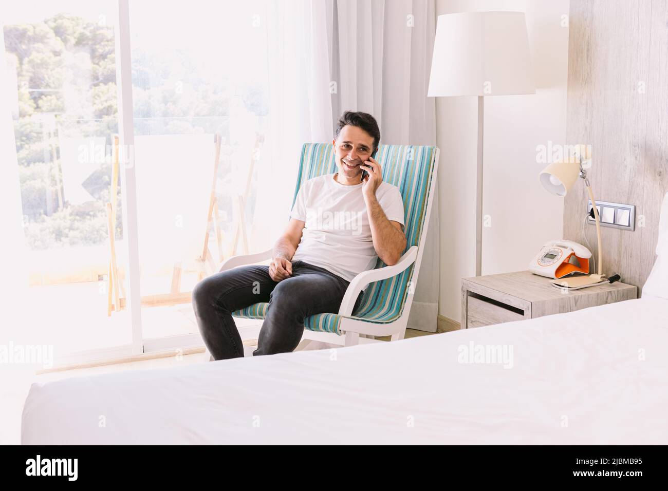 Young man sitting in a rocking chair in his bedroom, talking on the ...