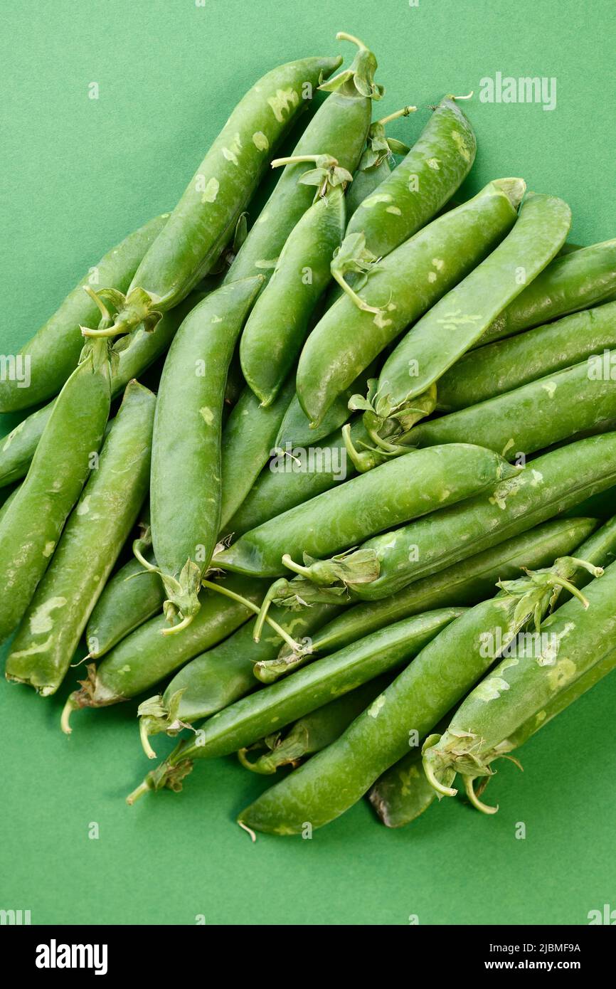 A pile of peas in pods on a green background Stock Photo - Alamy