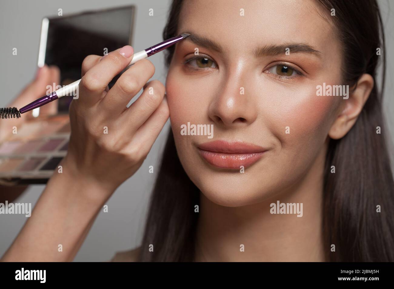 Makeup artist applies brown color shadow to a eyebrow of brunette woman ...