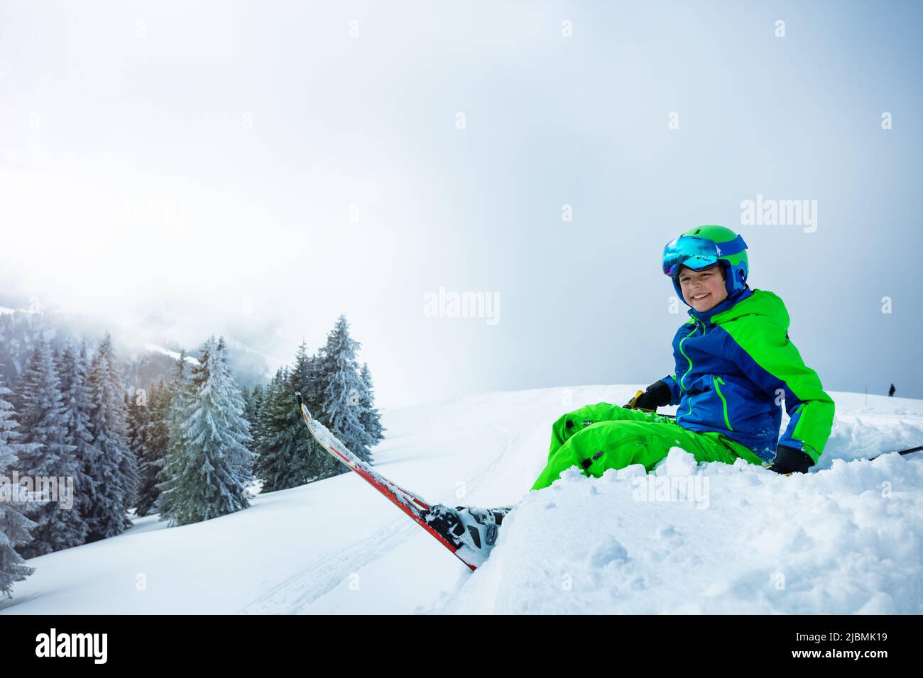 Boy with alpine skies sit in the snow and smile, side view Stock Photo ...