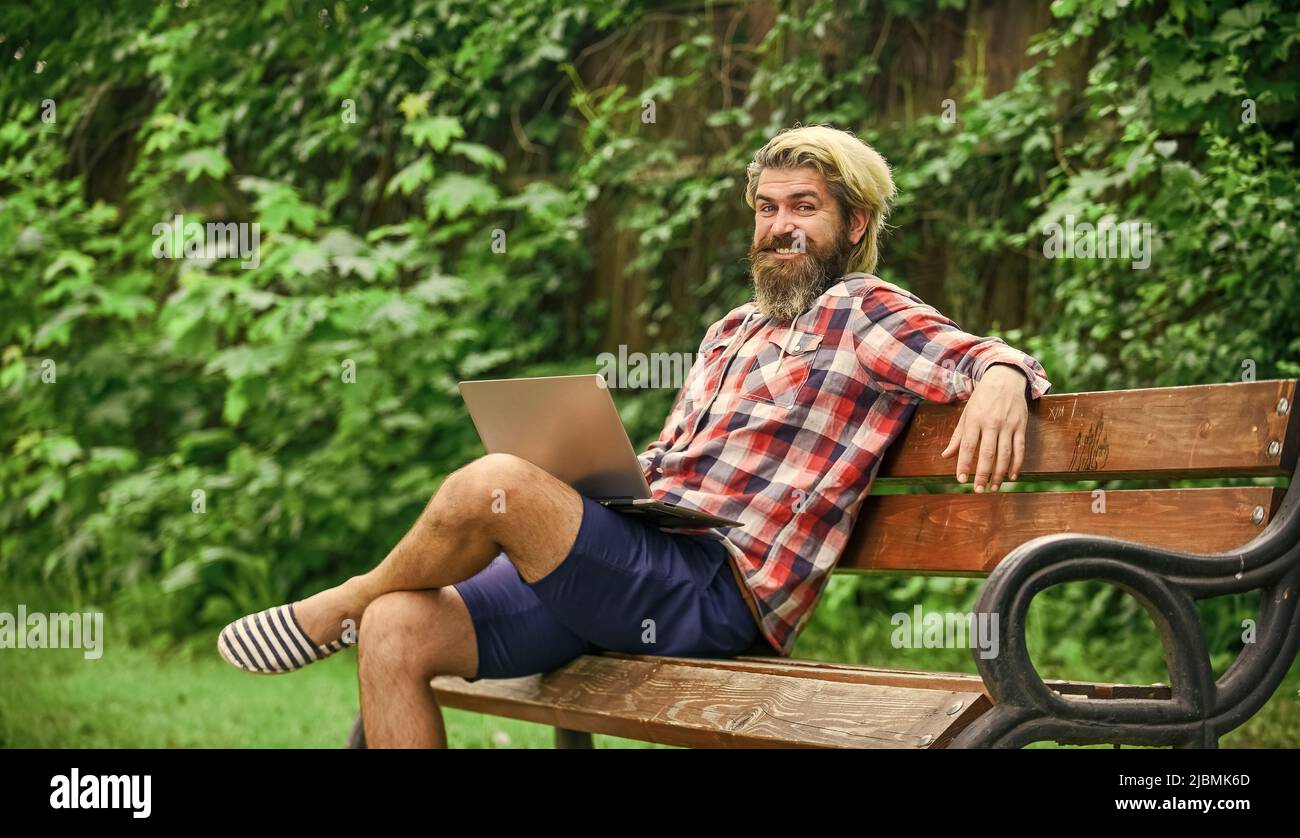 Really busy. mature man sitting on park bench with laptop and checking ...