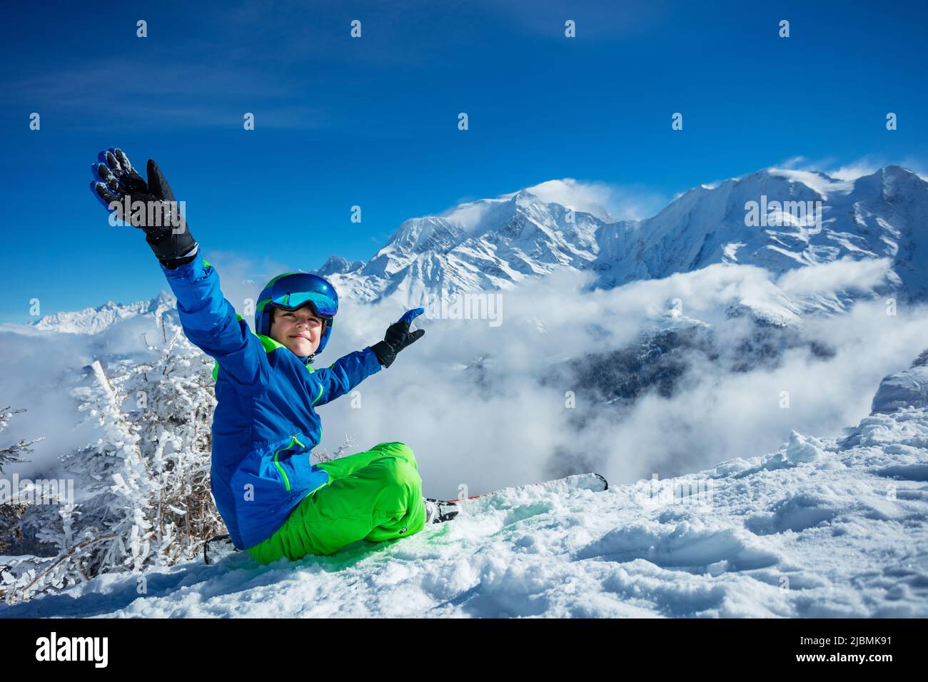 Smiling boy with alpine ski and helmet sit in snow lifting hands Stock ...