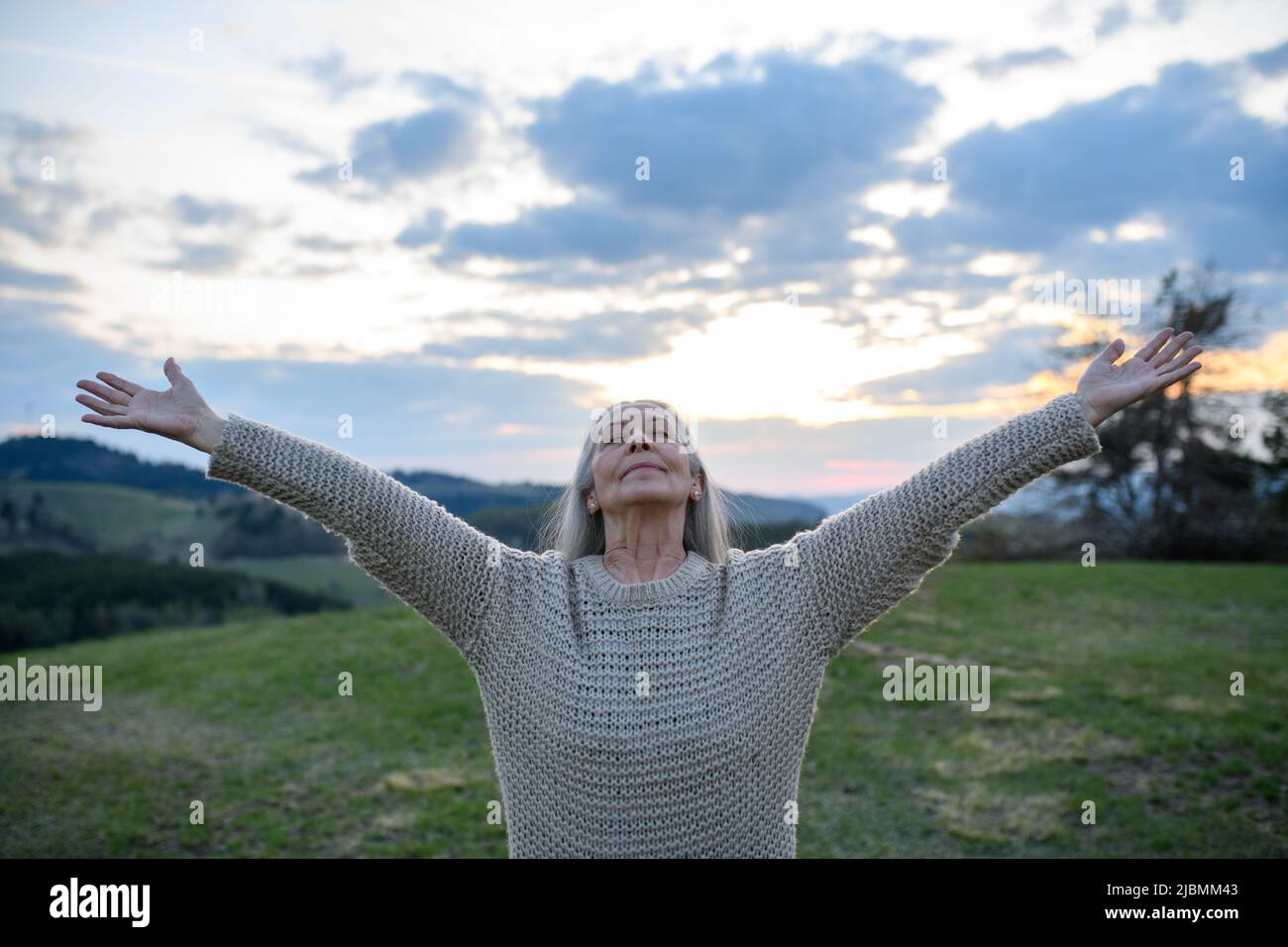 Senior woman with arms outstretched and face up at park on spring day ...