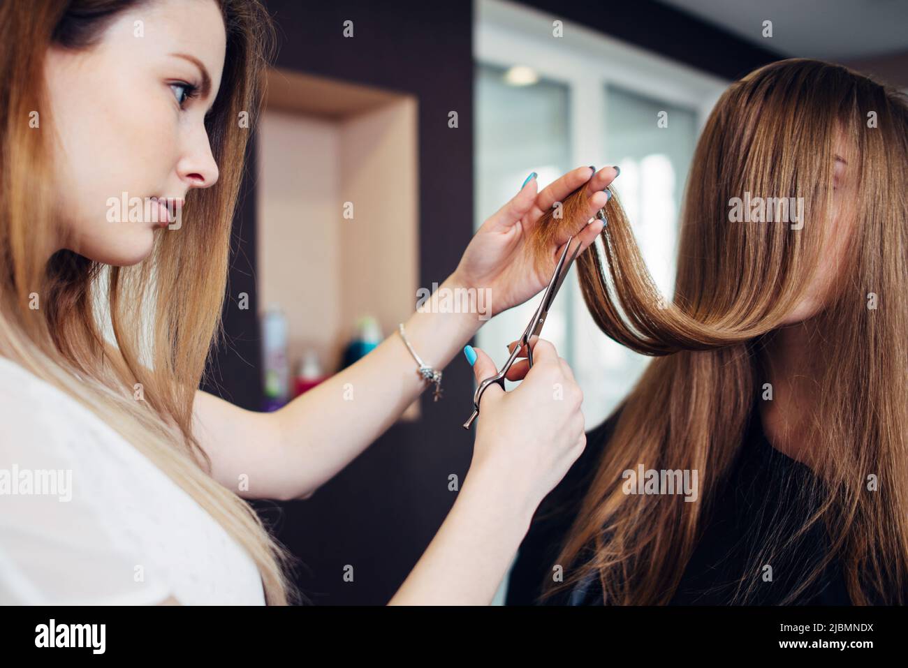 Hairdresser trimming the split ends of female customer sitting with ...