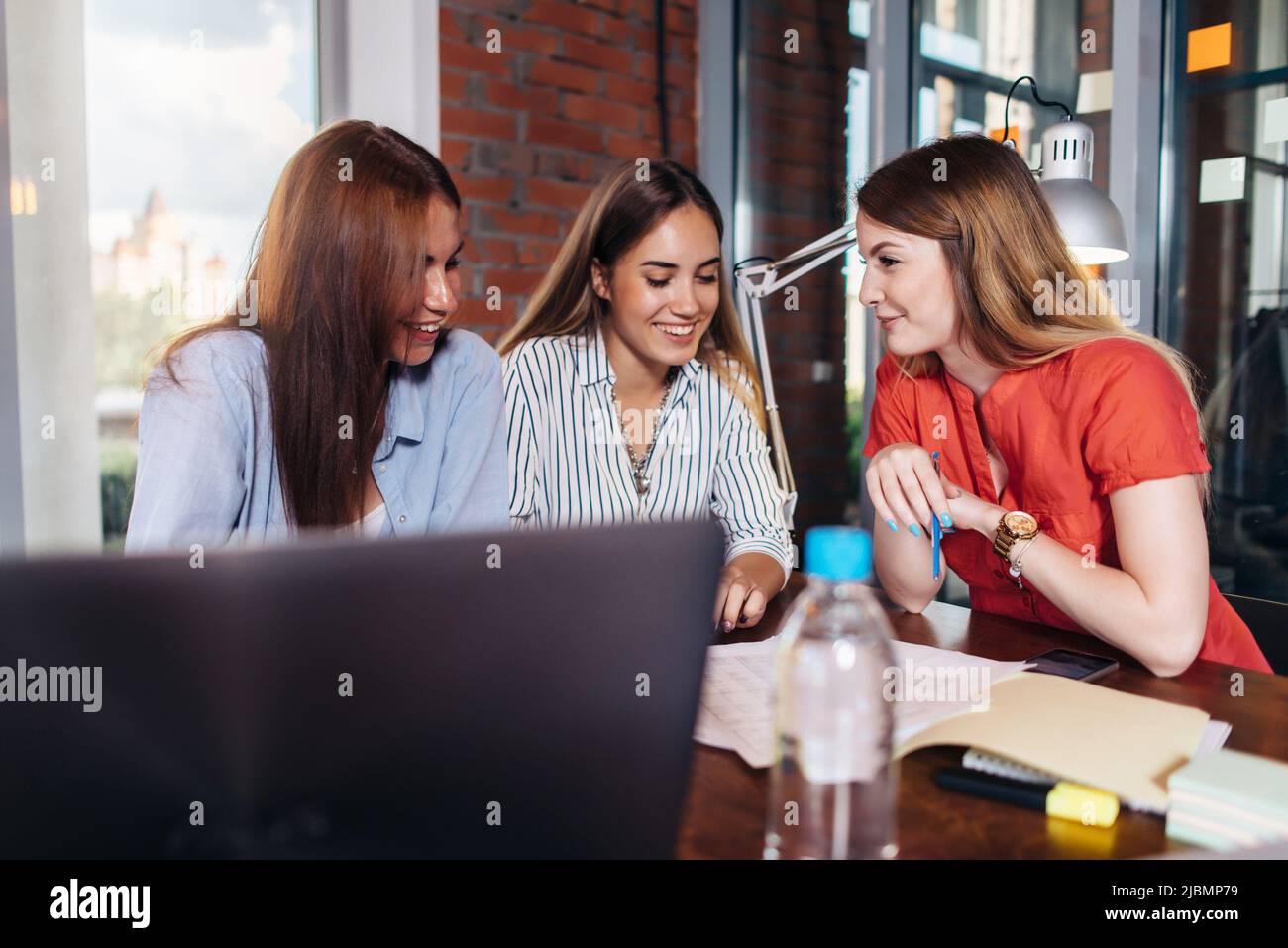 Three smiling female college students working on project together in ...