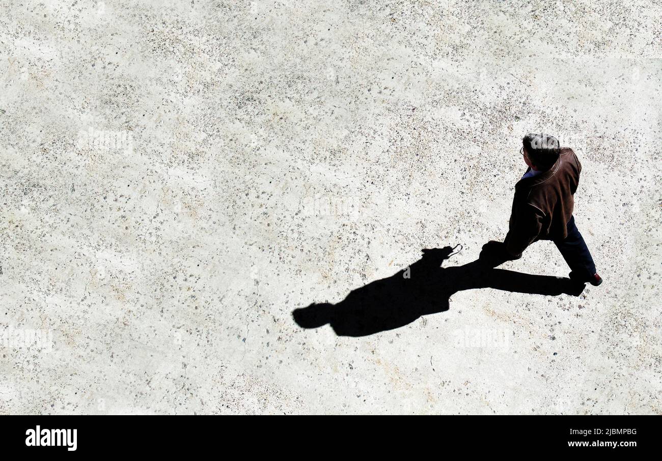 Man walking with dark shadow across cement walkway representing mystery ...