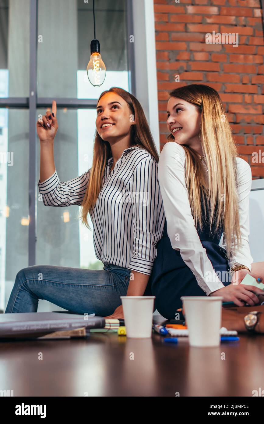 Two pretty female students sitting together on desk in classroom, a ...