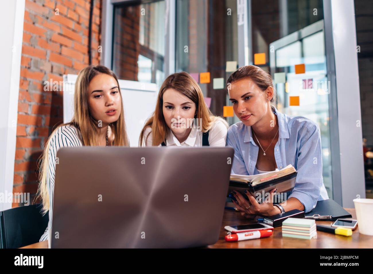 Three female college students studying together using laptop and ...