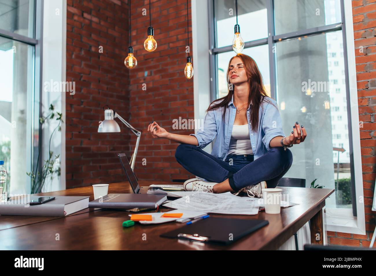 Female student sitting in lotus pose on table in her room meditating ...