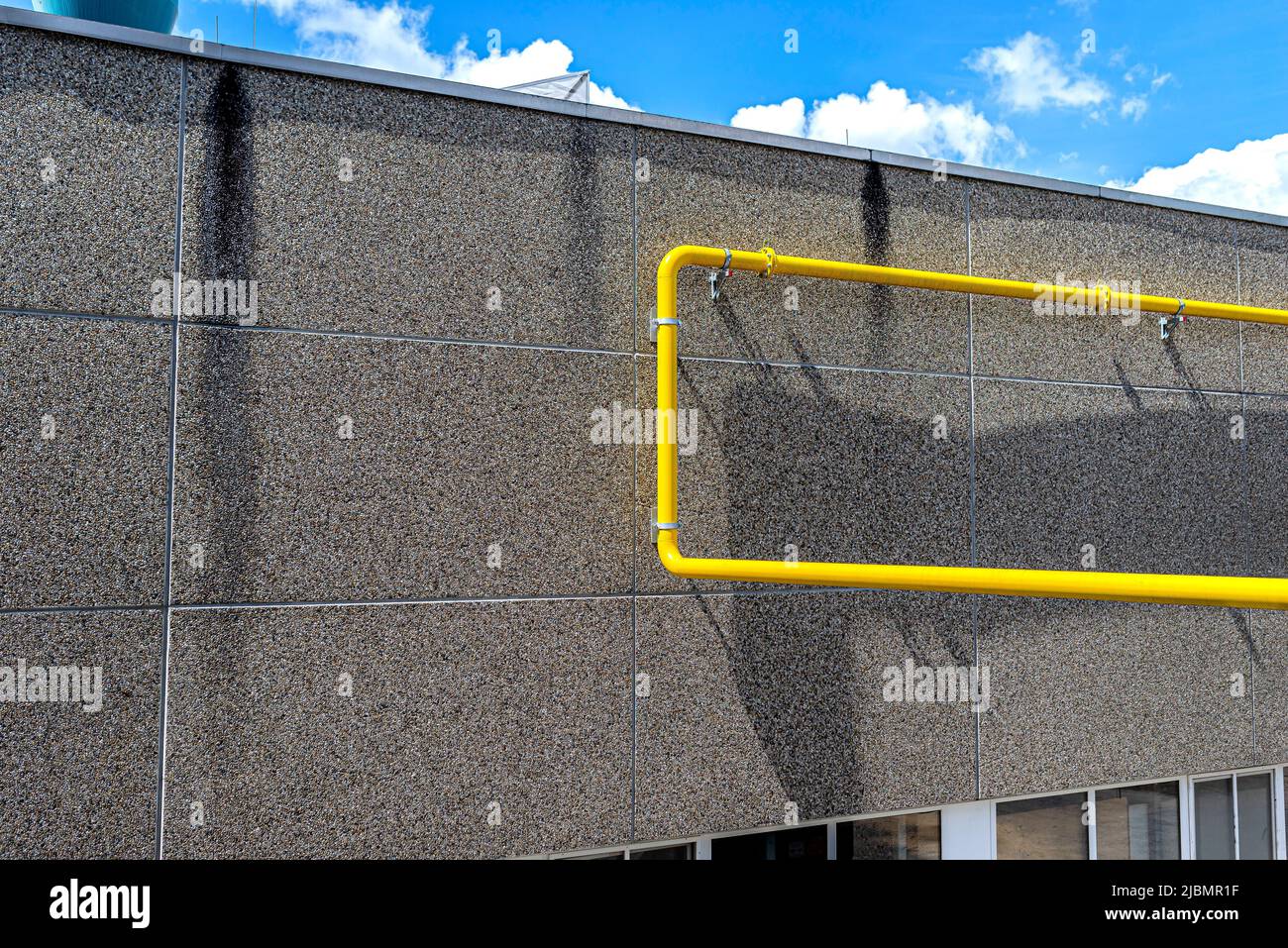 A large yellow gas pipe running up a factory wall made of concrete and ...
