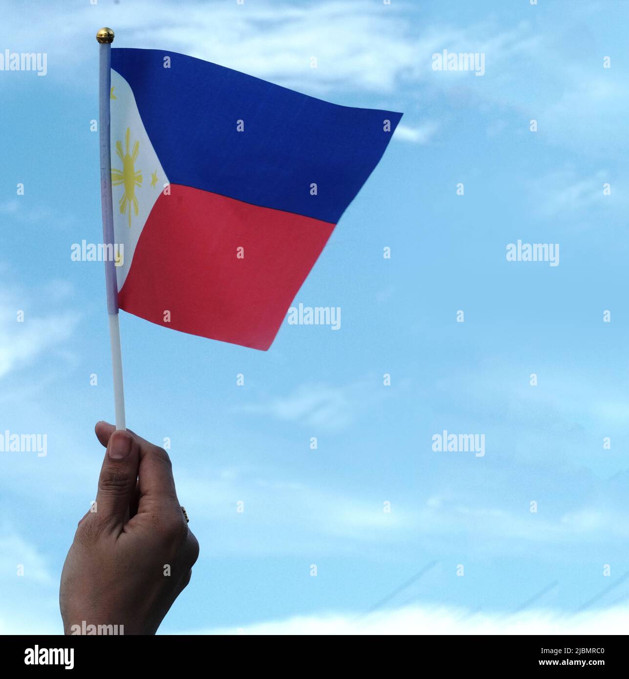 A hand waves a Philippine flag against a blue sky Stock Photo - Alamy