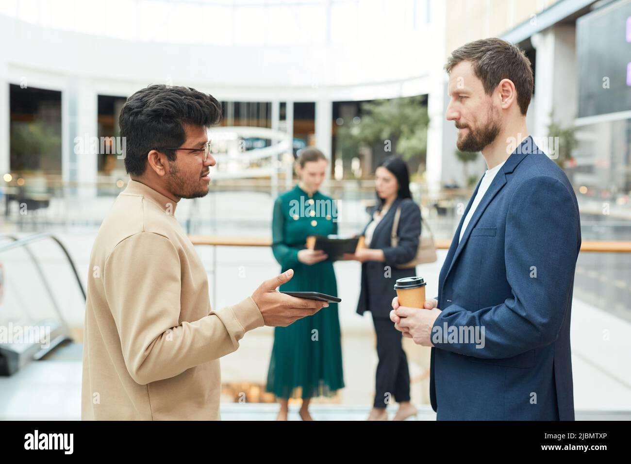 Side view portrait of two businessmen talking while standing in office ...