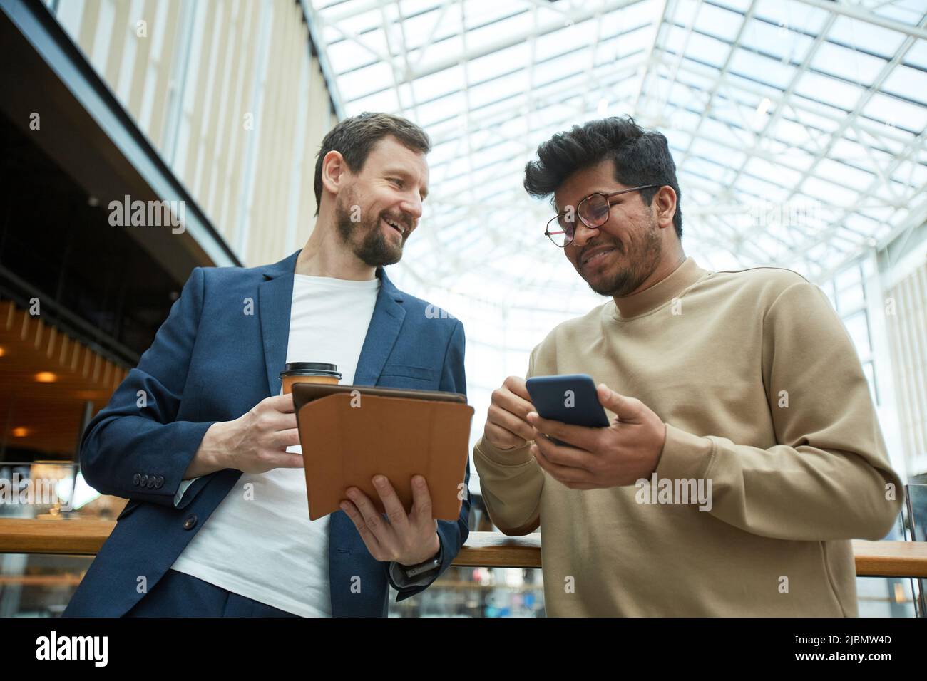 Low angle portrait of two smiling men communicating and holding mobile ...