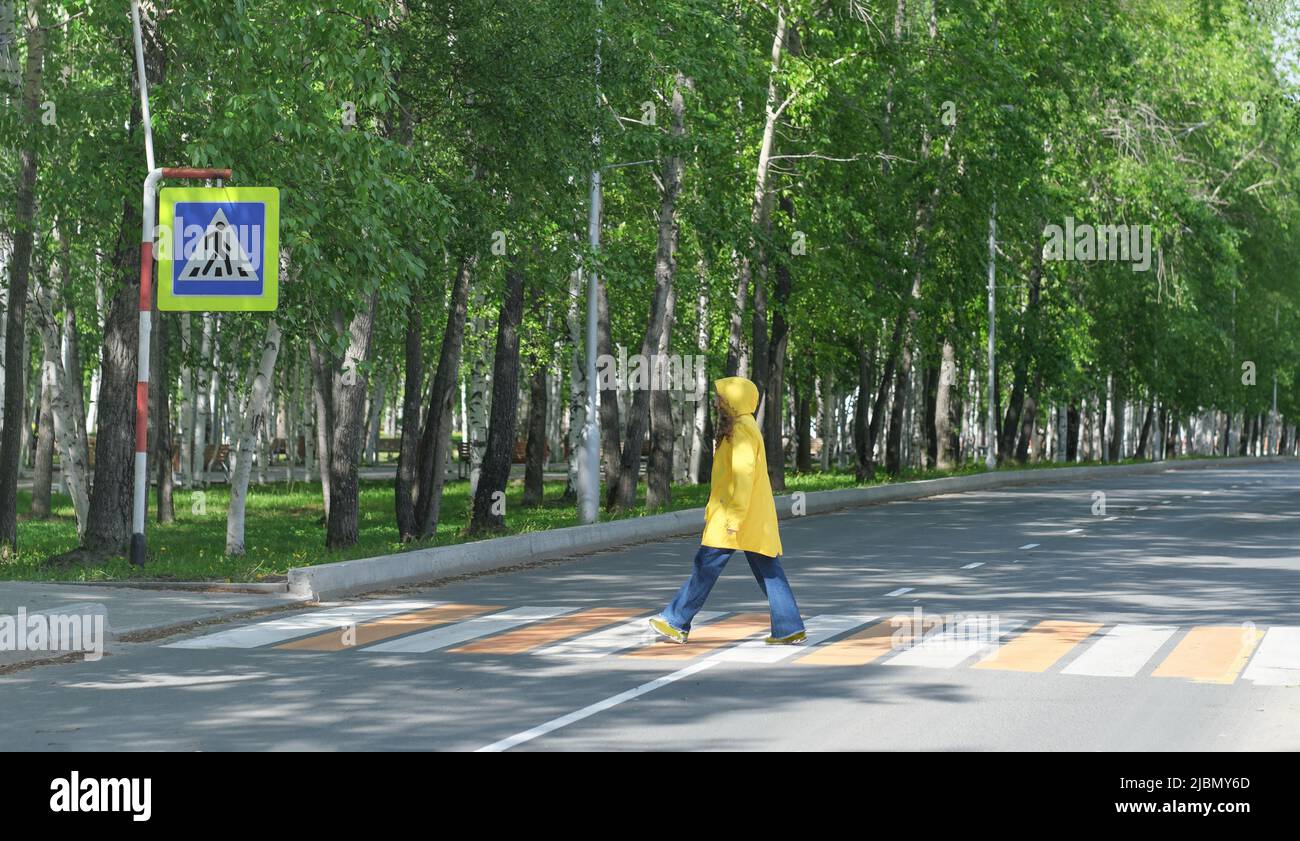 Teenager girl wearing yellow rain jacket comes across the street ...