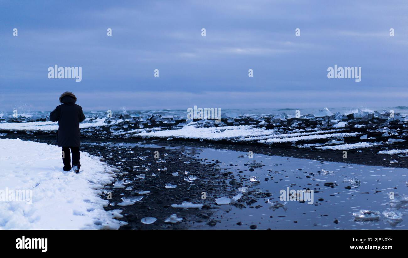 A man in a winter coat walking down diamond beach, a beach littered ...