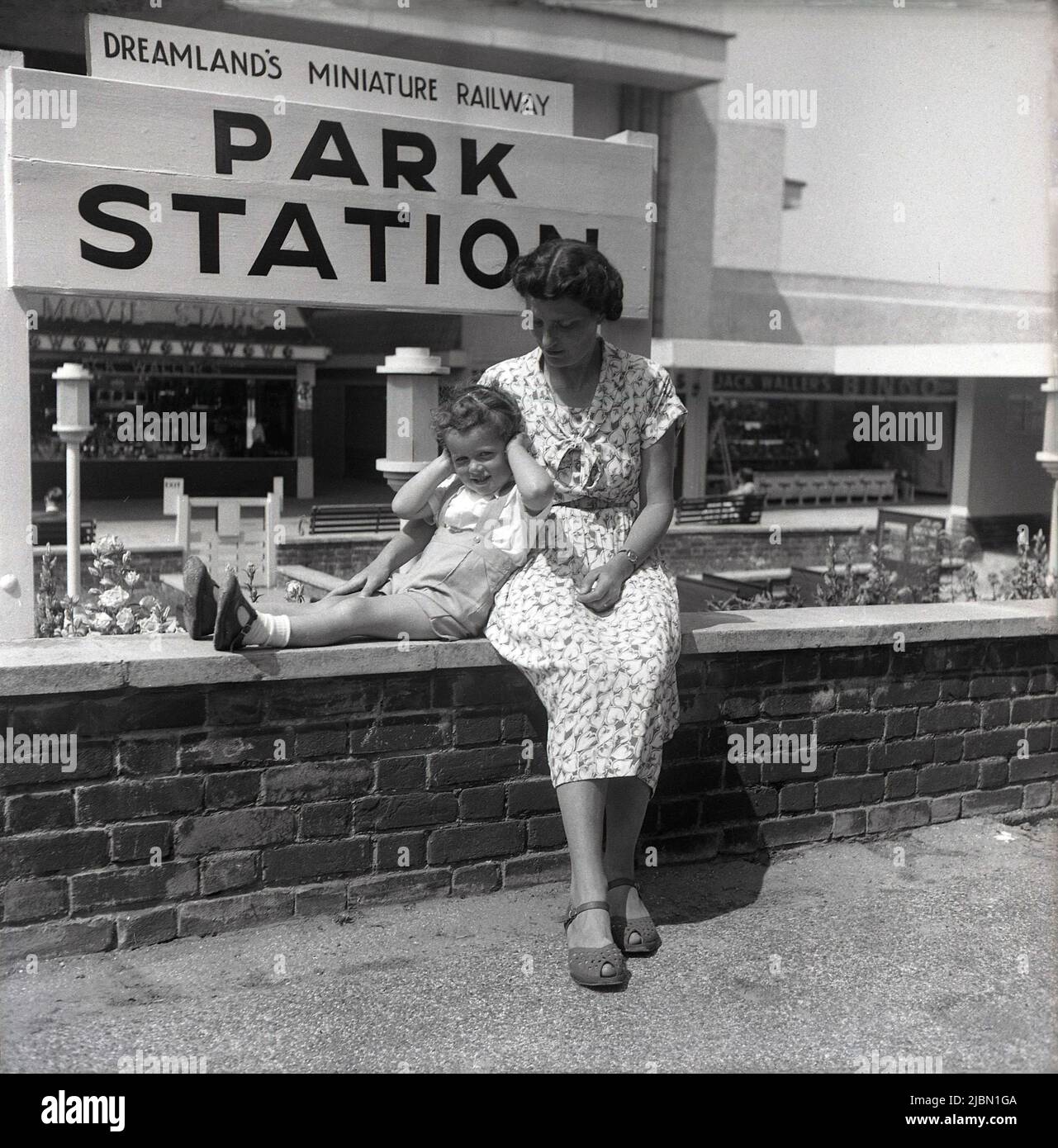 1950s, historical, a mother and her young son sitting on a small wall ...