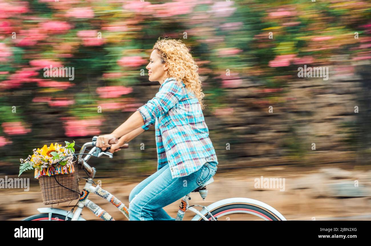 Happy adult woman ride a bike outdoor with flowers in background ...