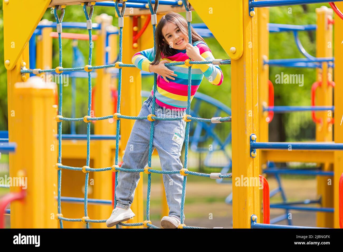 little cute girl 5-6 years old stands on a rope ladder, on a childrens ...