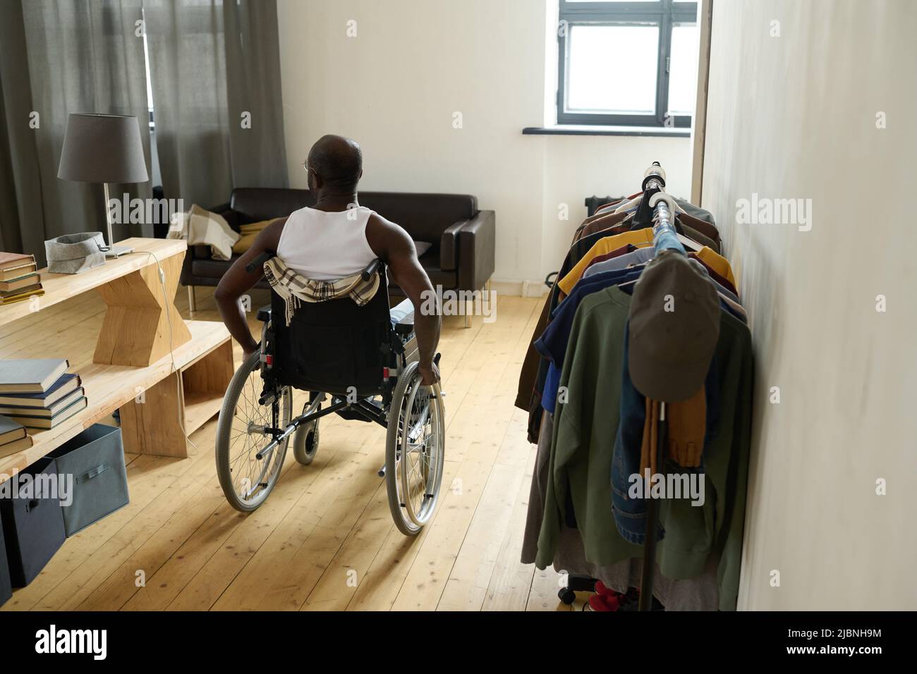 Rear view of man with disability riding along the room in wheelchair ...
