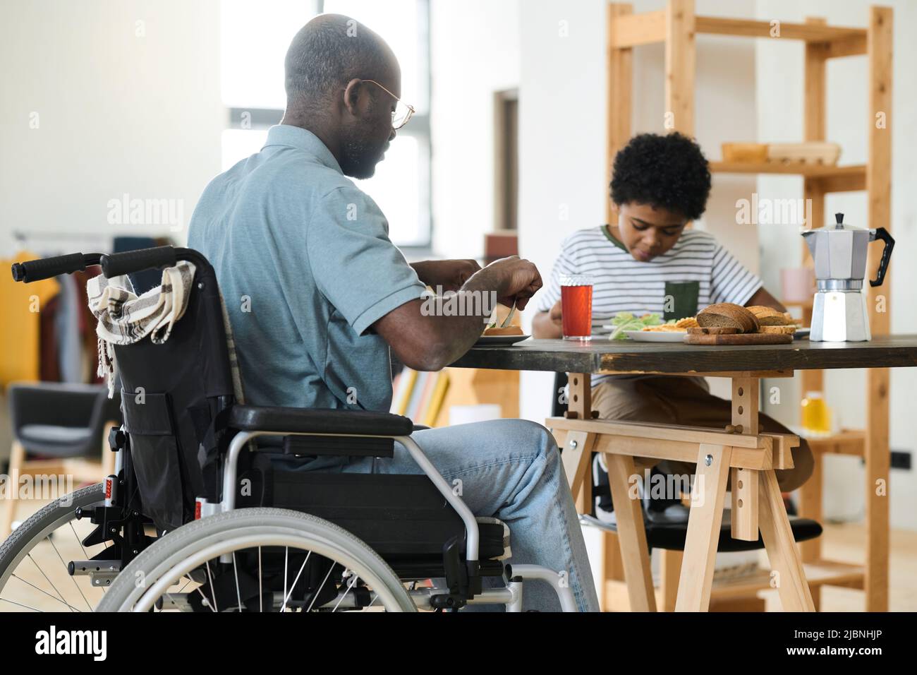 Rear view of disabled father sitting in wheelchair at table and having ...