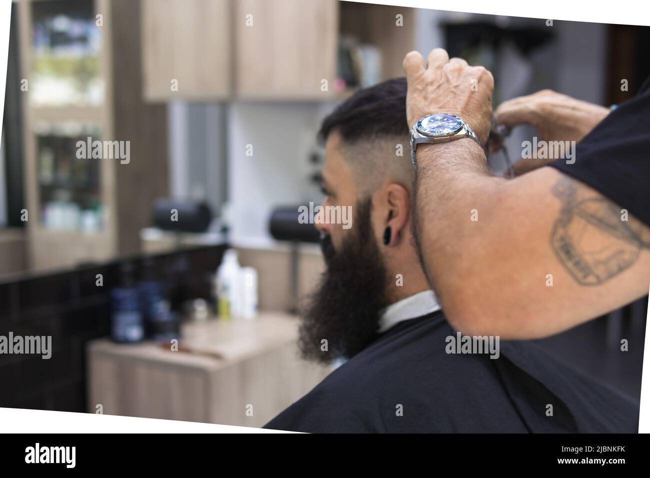 Bearded client getting a haircut by a tattooed barber inside barber ...