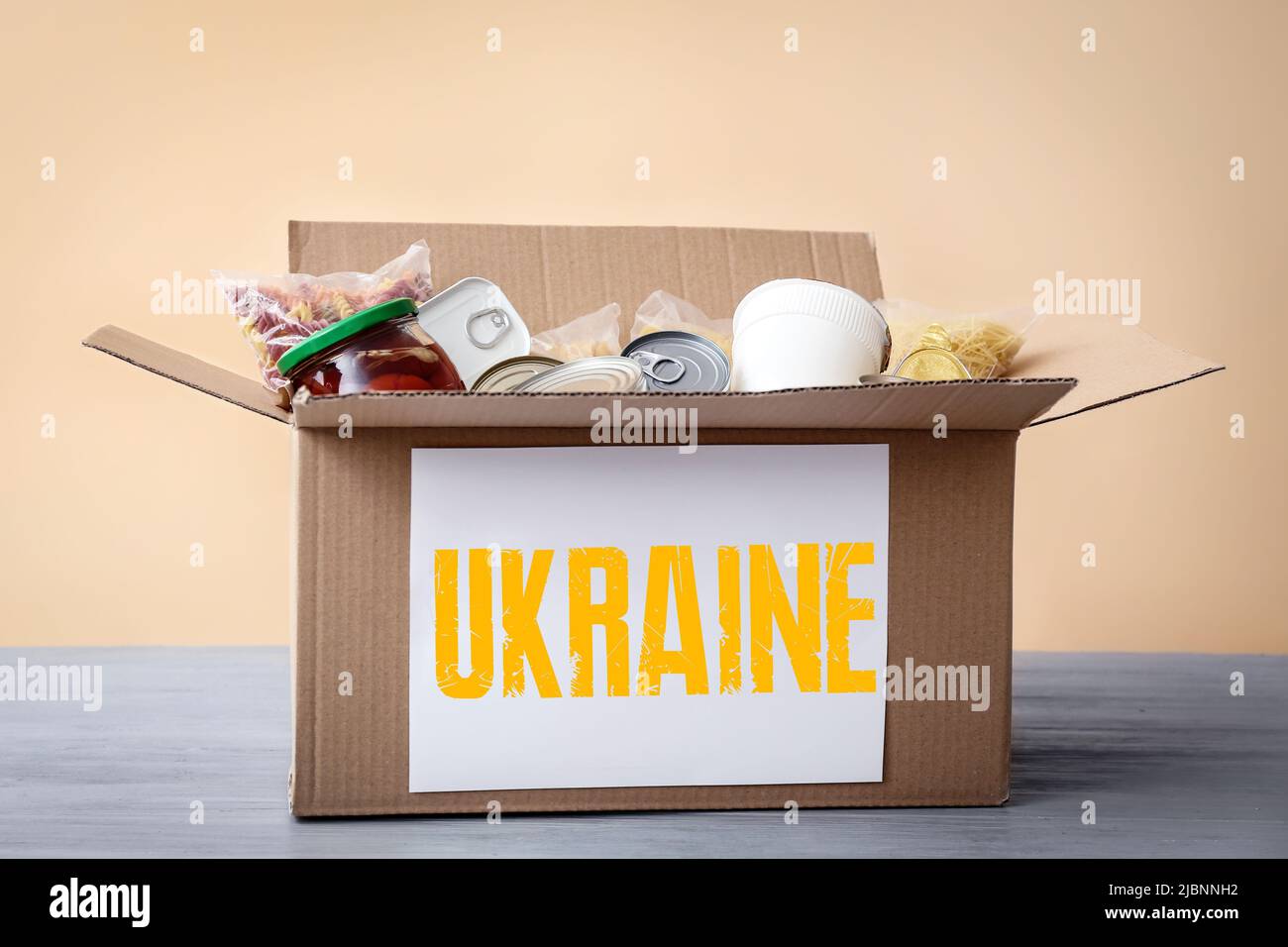 Box with food on table against color background. Humanitarian aid for ...