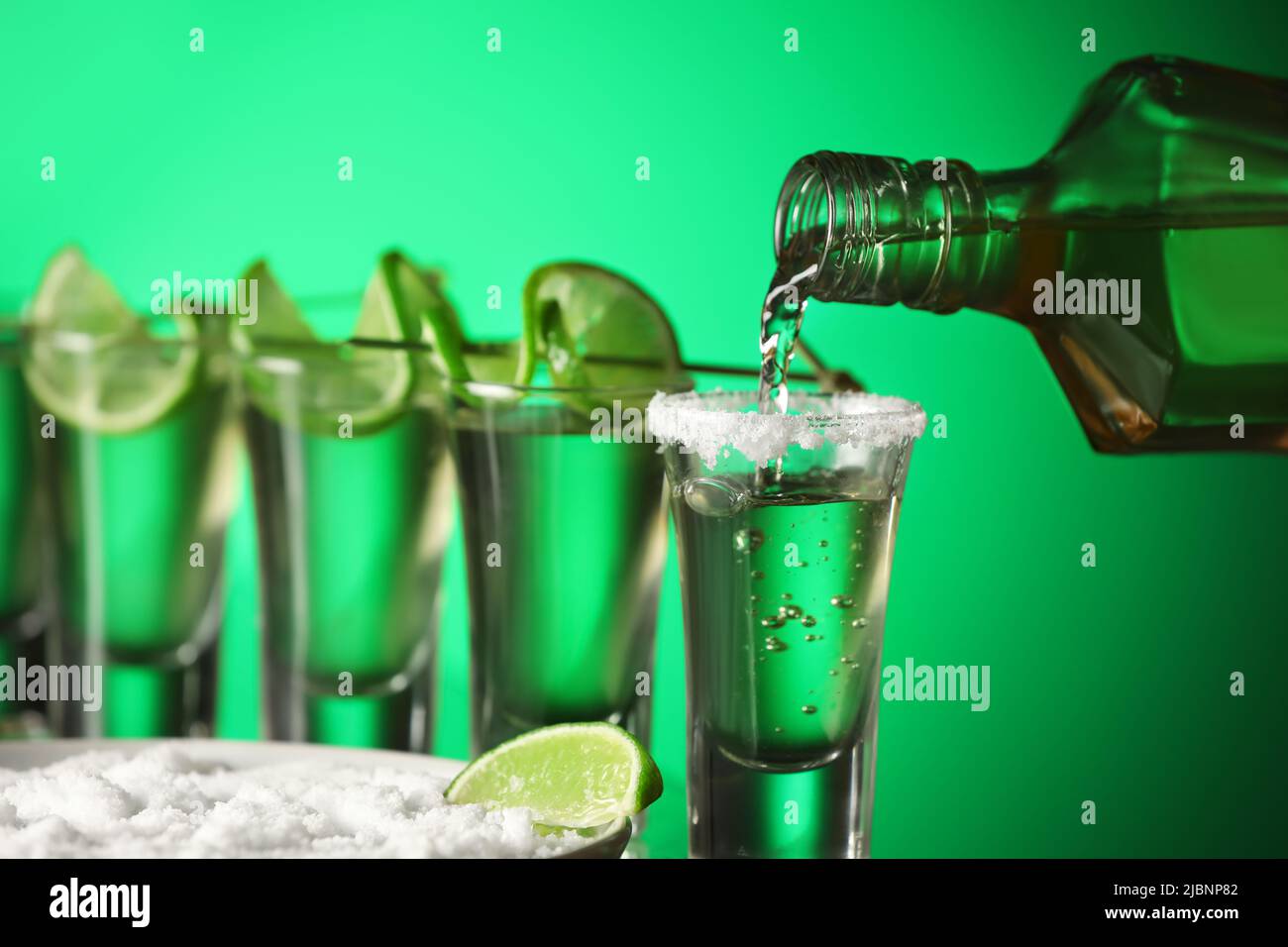 Pouring of tasty mexican tequila from bottle into shots on color ...