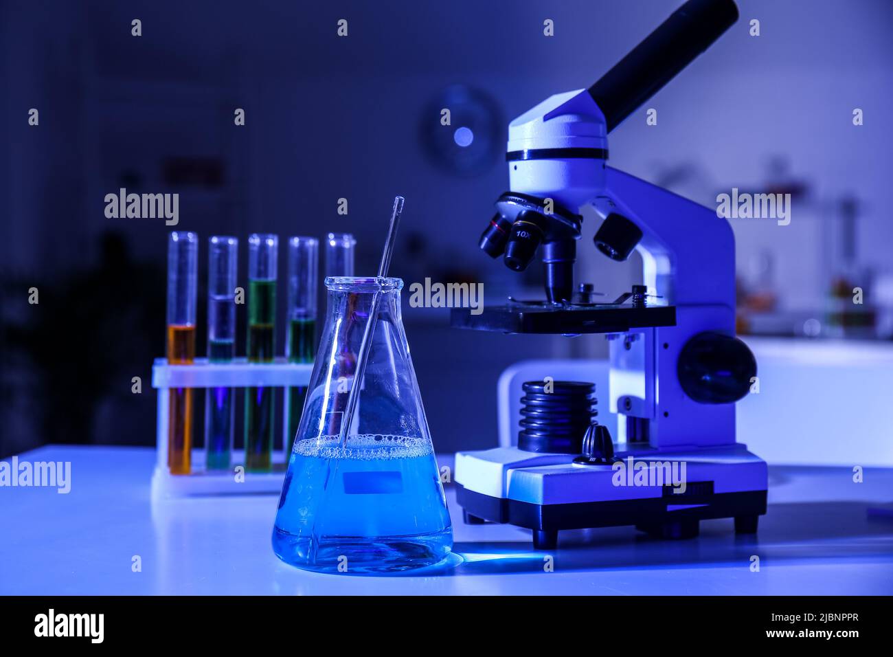Modern microscope and conical flask with liquid on table in medical ...