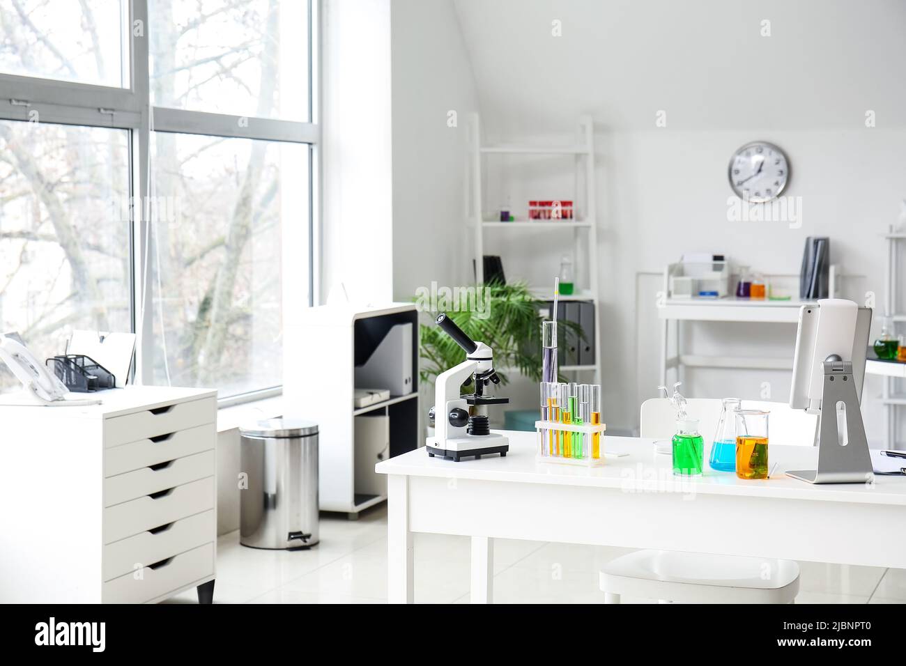 Microscope, tablet computer and chemical glassware on table in medical ...