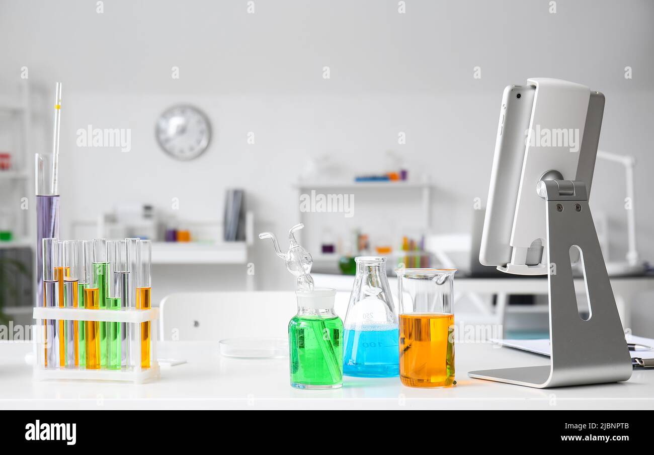 Microscope, tablet computer and chemical glassware on table in medical ...
