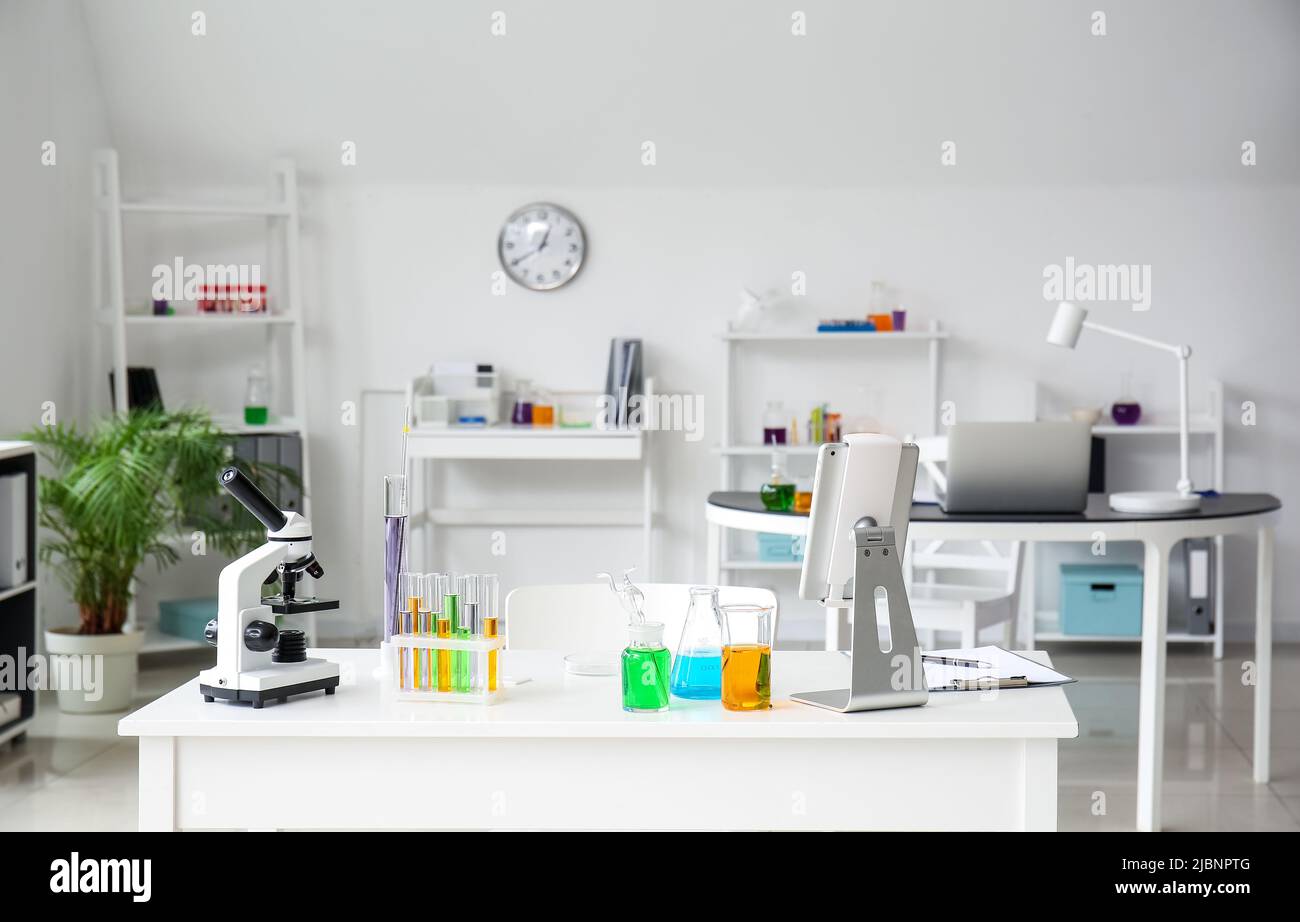 Microscope, tablet computer and chemical glassware on table in medical ...