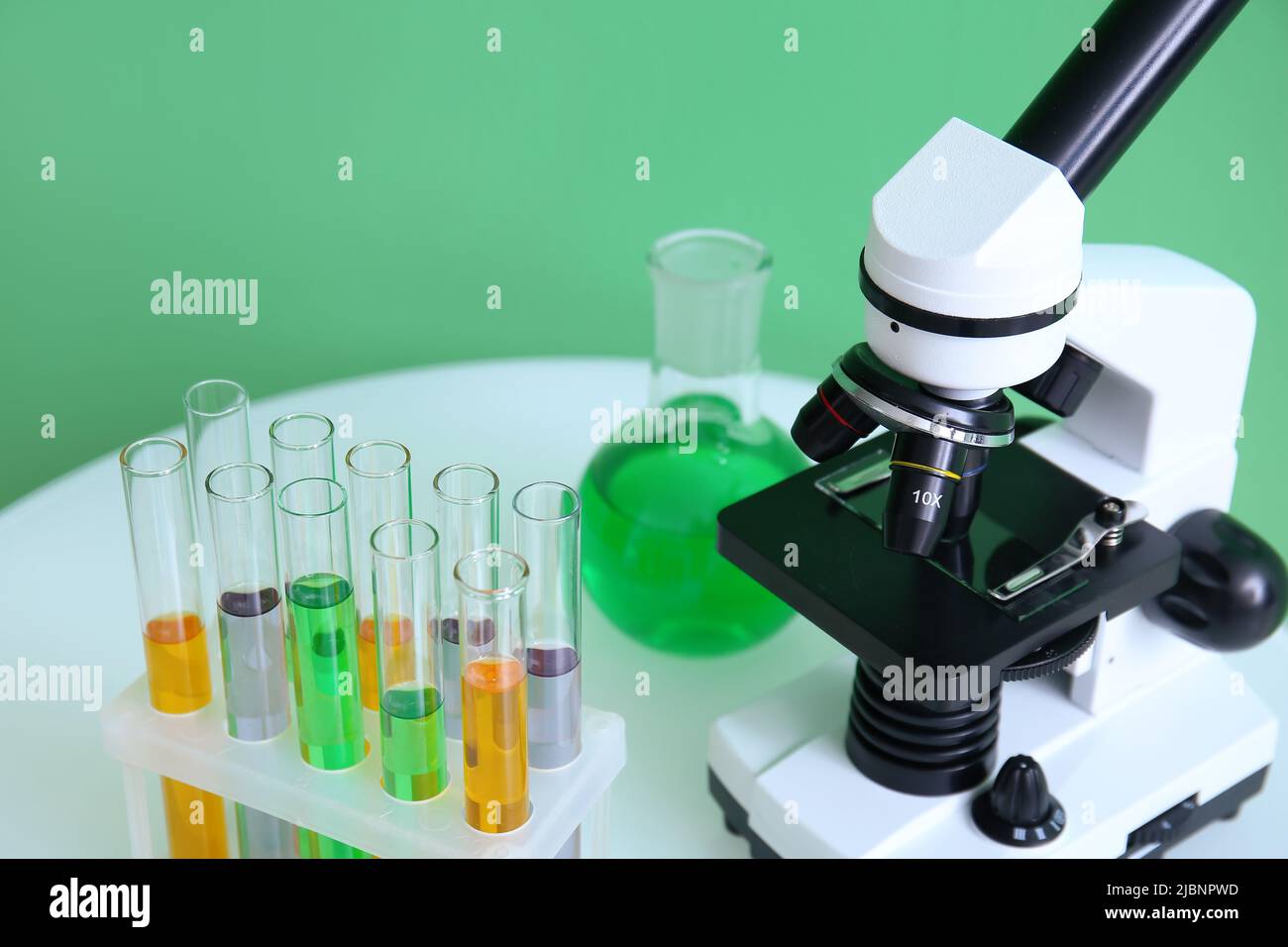 Modern microscope and test tubes with samples on table near green wall ...