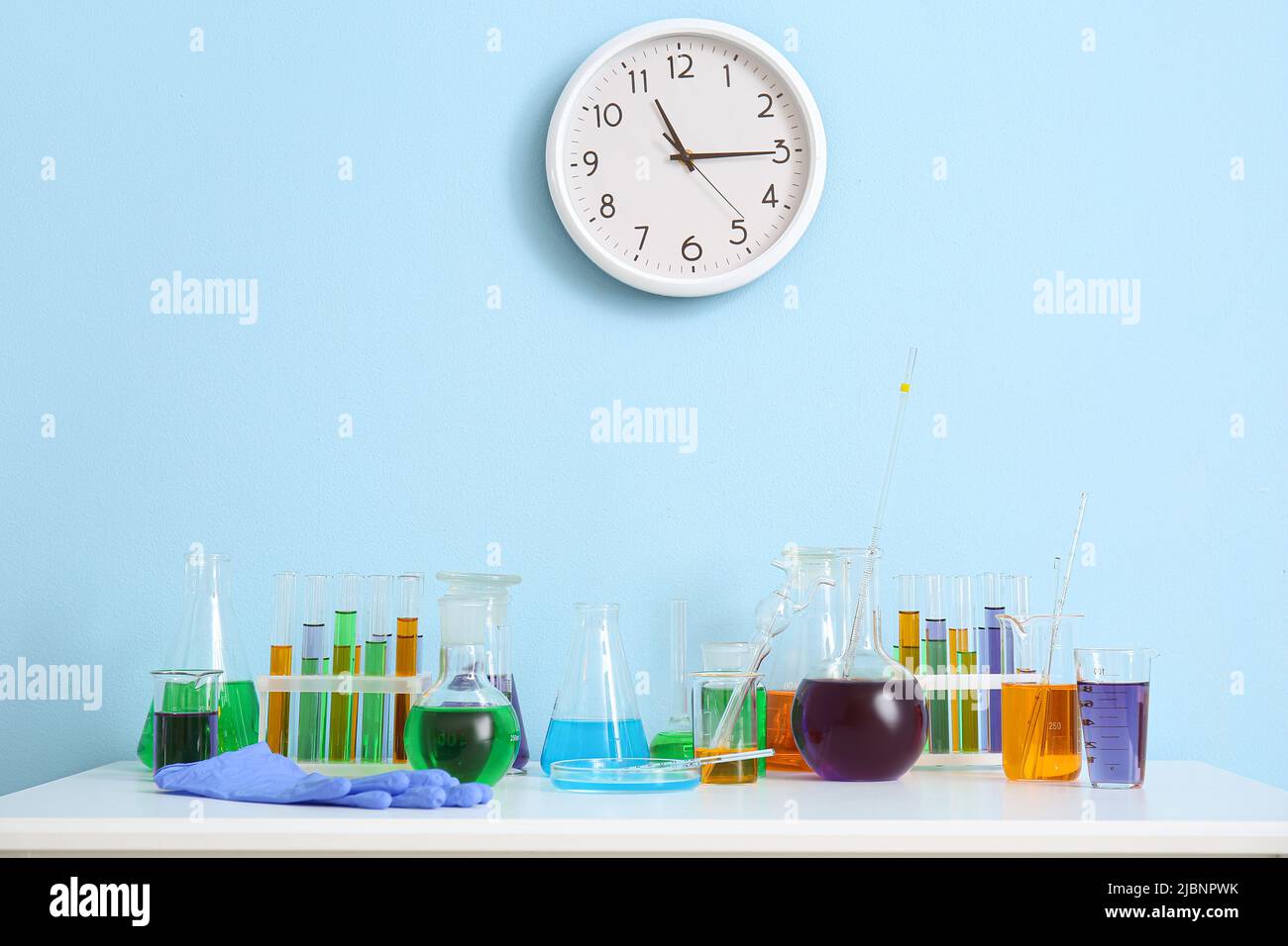 Different laboratory glassware with samples on table near blue wall ...