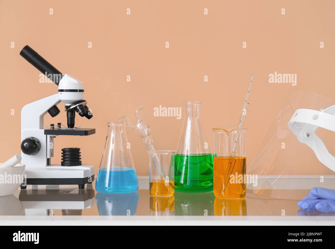 Modern microscope and laboratory glassware with liquid on table near ...