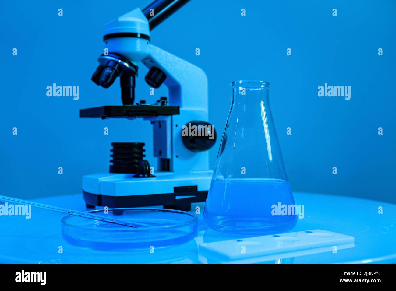Different laboratory glassware with samples and microscope on table ...